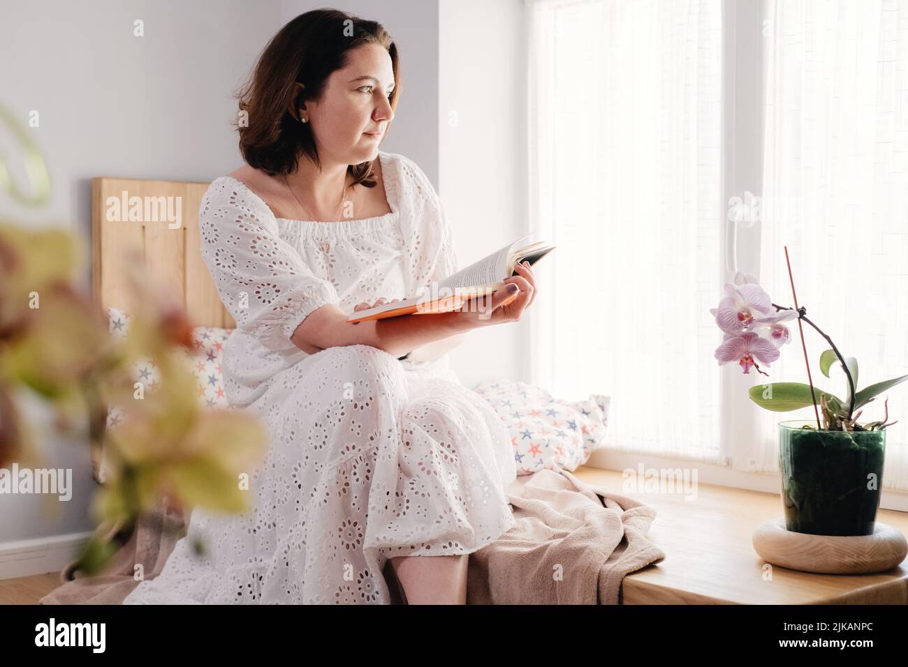 Mid age adult woman plus size reading a book by the window on the ...