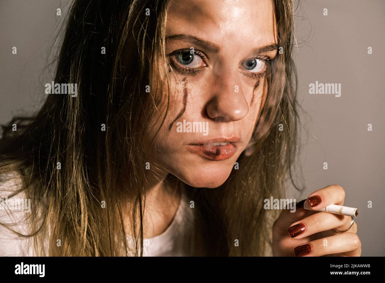 Crying young woman with cigarette in her hand and abrasions on her face ...