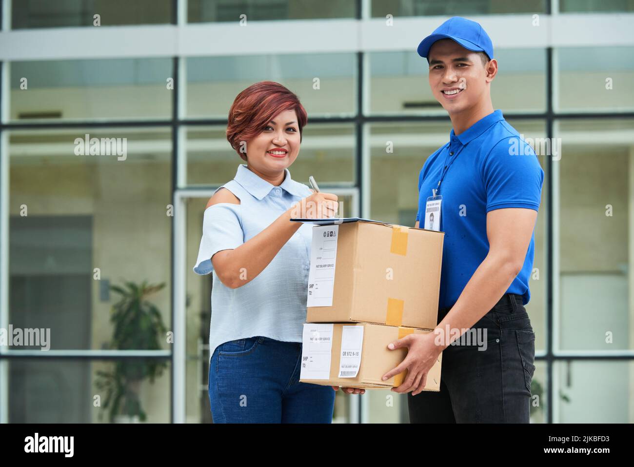 Cheerful Asian woman signing document when receiving packages Stock ...