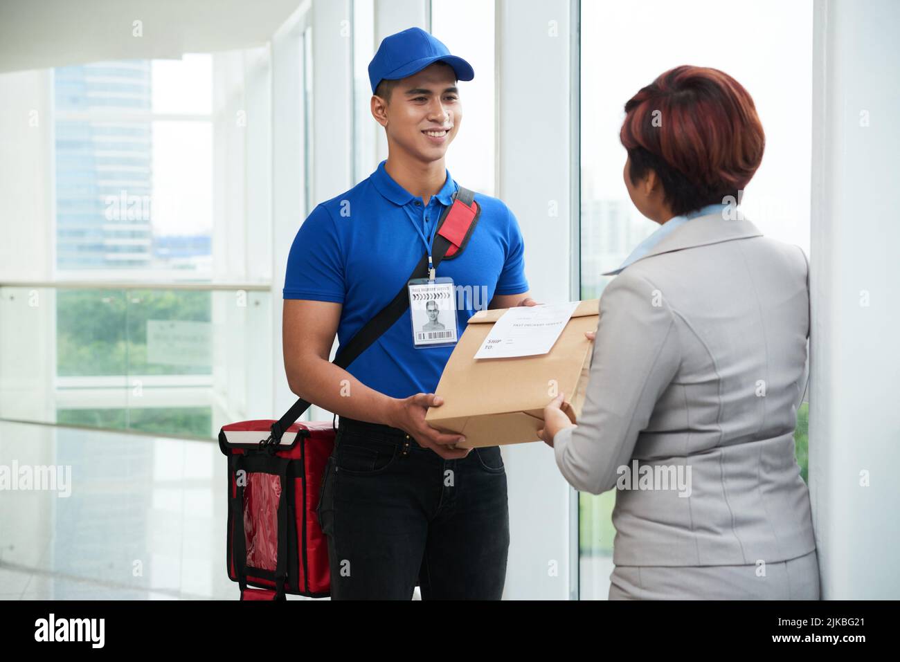 Smiling Asian delivery man bringing package to business lady Stock ...
