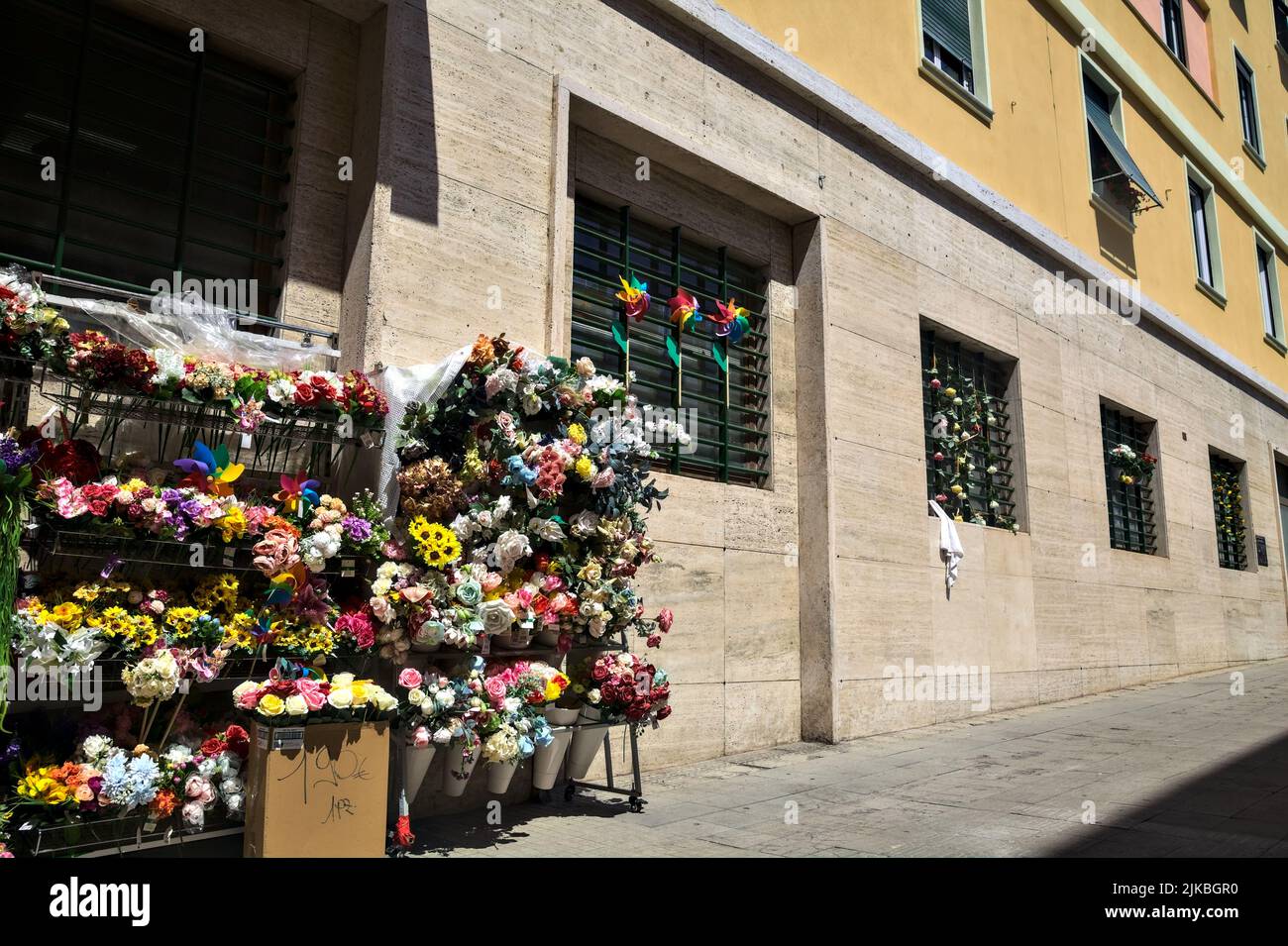 Shop racks with fake flowers and pinwheels on the pavement of a street ...