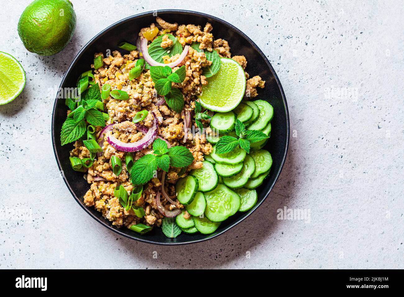 Thai chicken salad larb gai with onion, cucumber and mint in a black ...