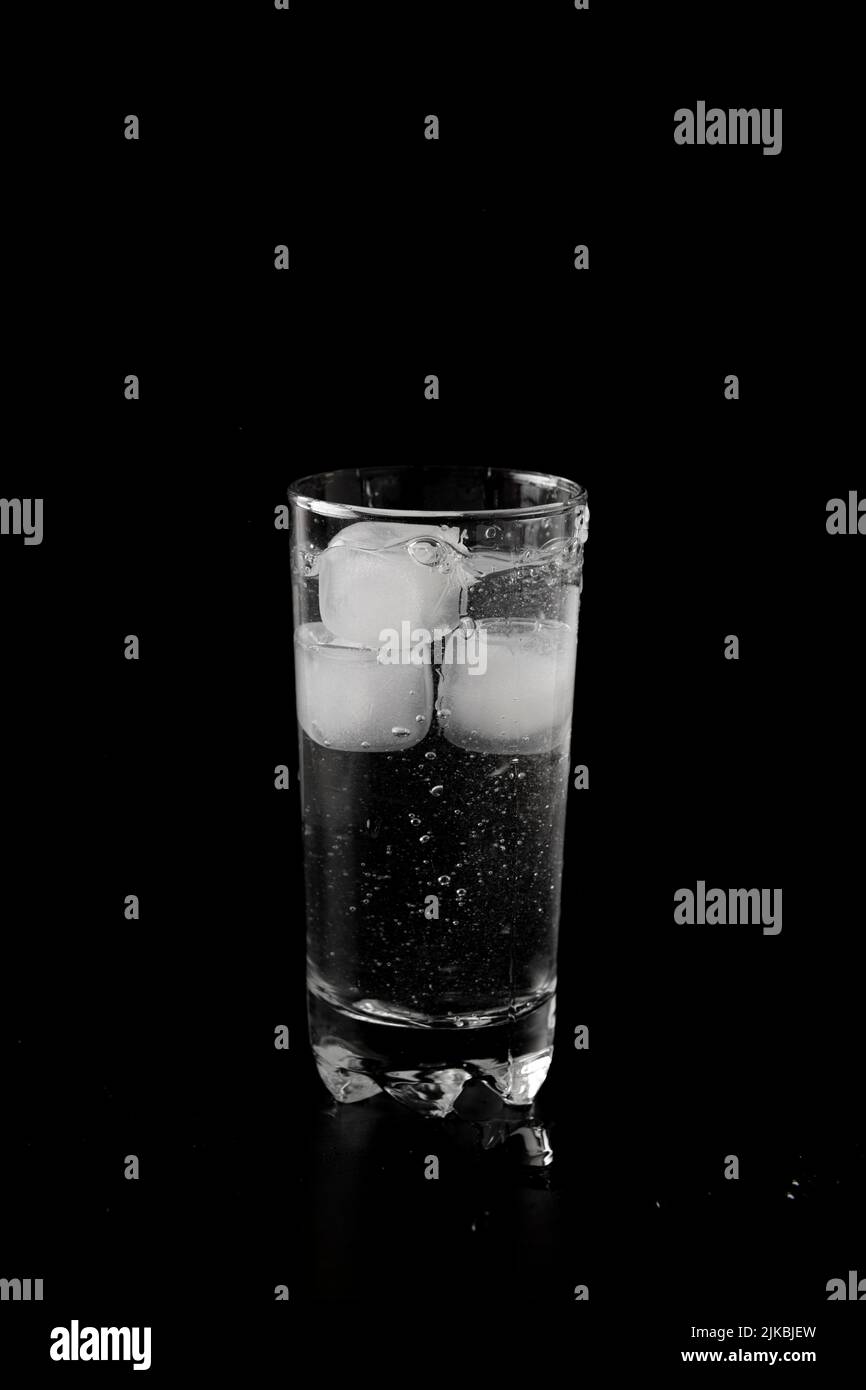Ice cubes thrown to a glass of water from above with splash on a black ...