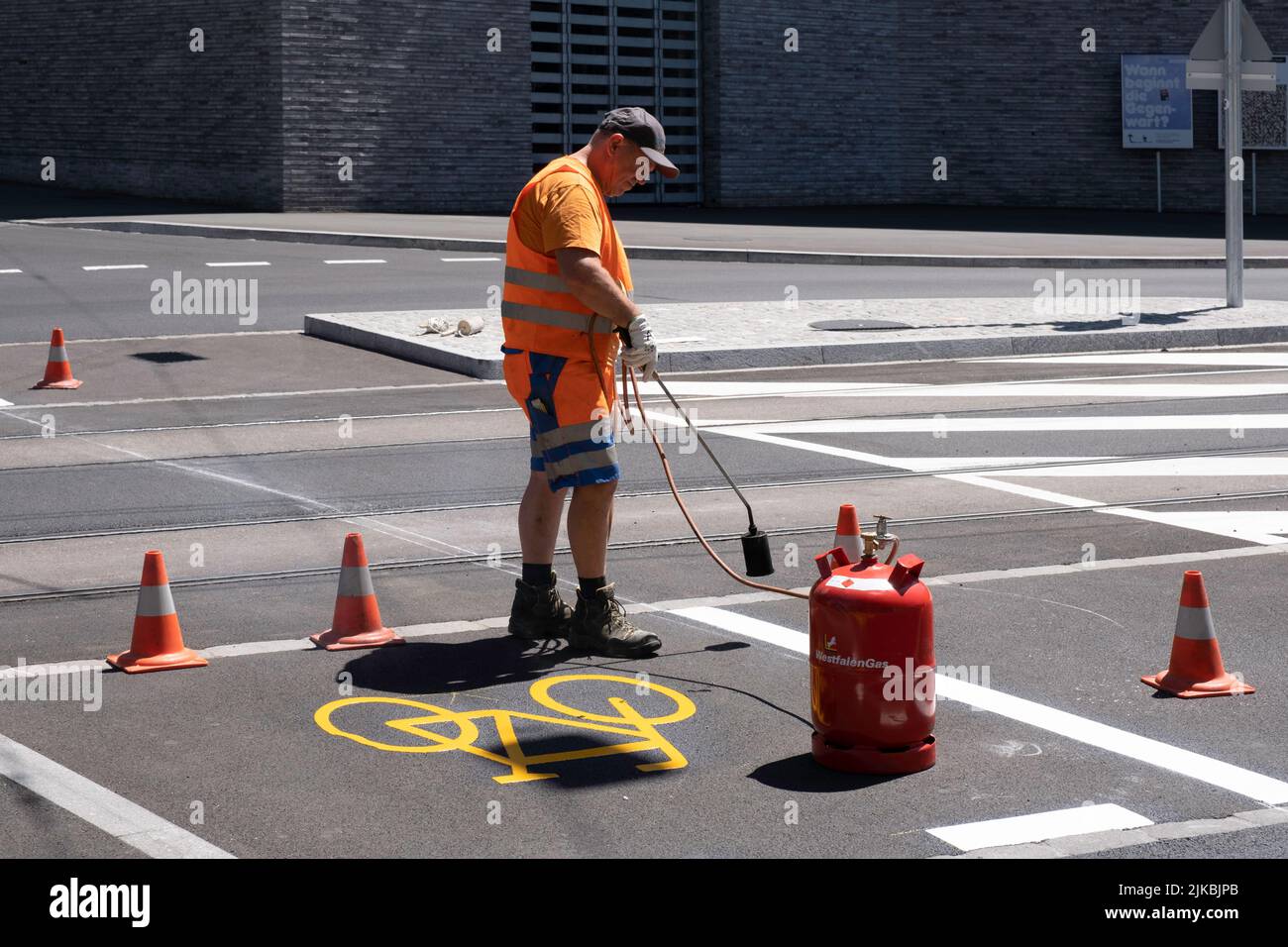 Road worker with safety vest uses a gas blow torch to heat the asphalt ...