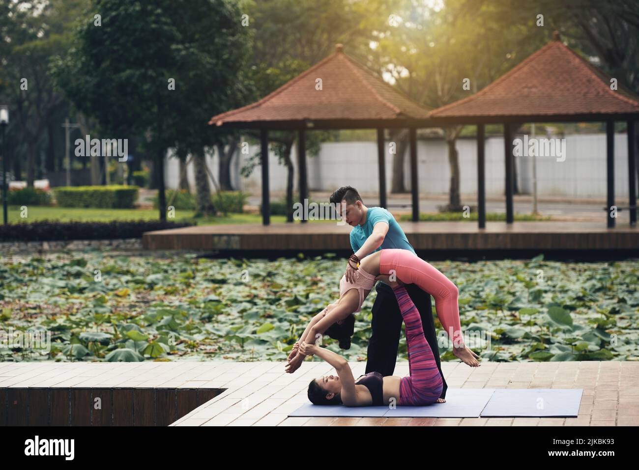 Vietnamese young instructor helping women to perform partner yoga pose ...