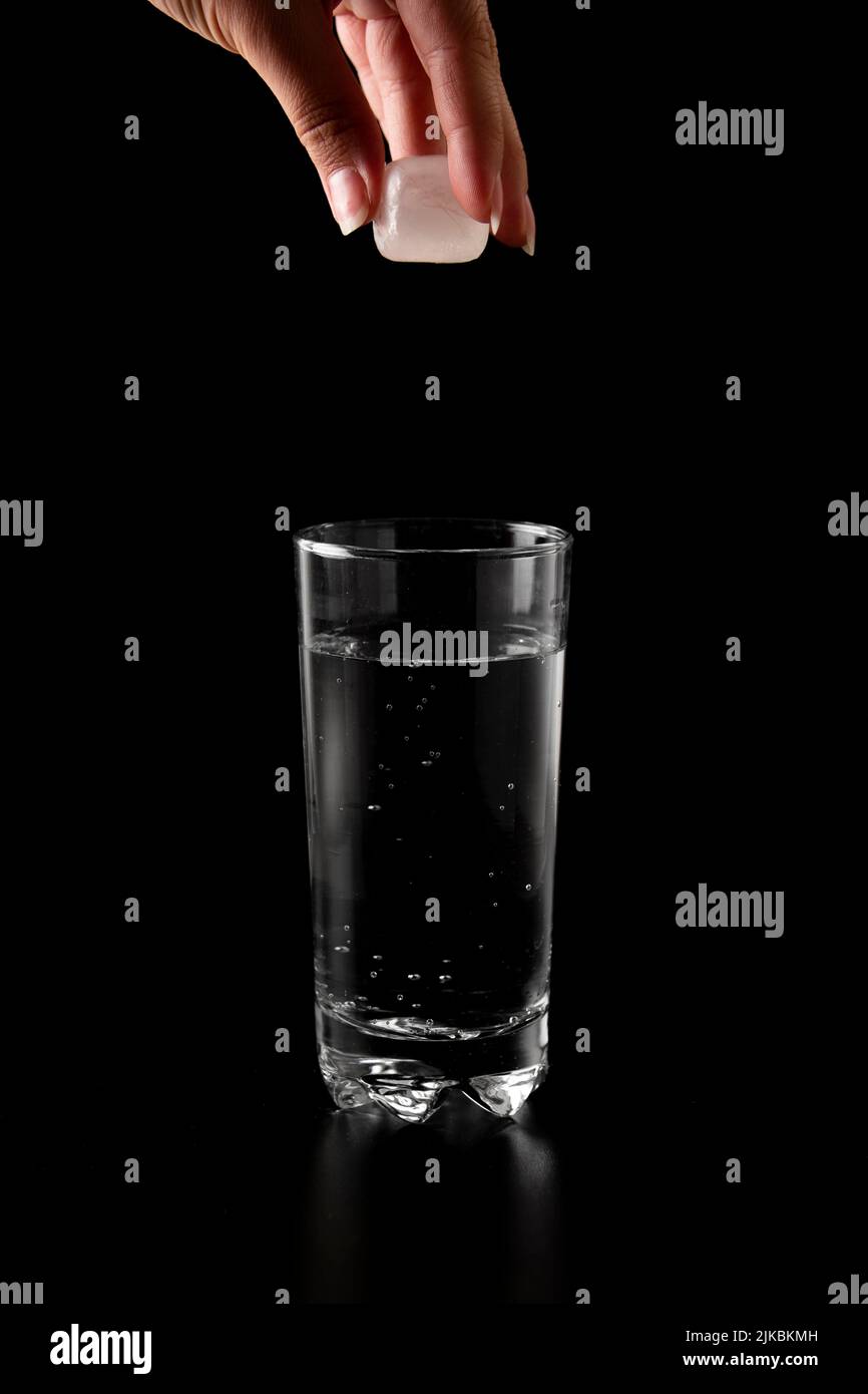 Ice cubes thrown to a glass of water from above with splash on a black ...