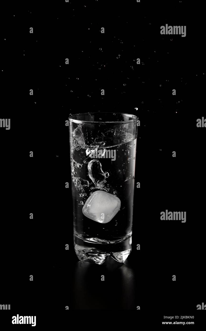 Ice cubes thrown to a glass of water from above with splash on a black ...