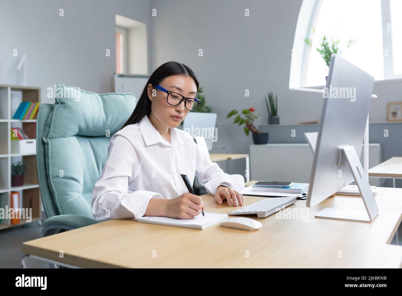 Young beautiful Asian woman secretary making notes in notebook with pen ...
