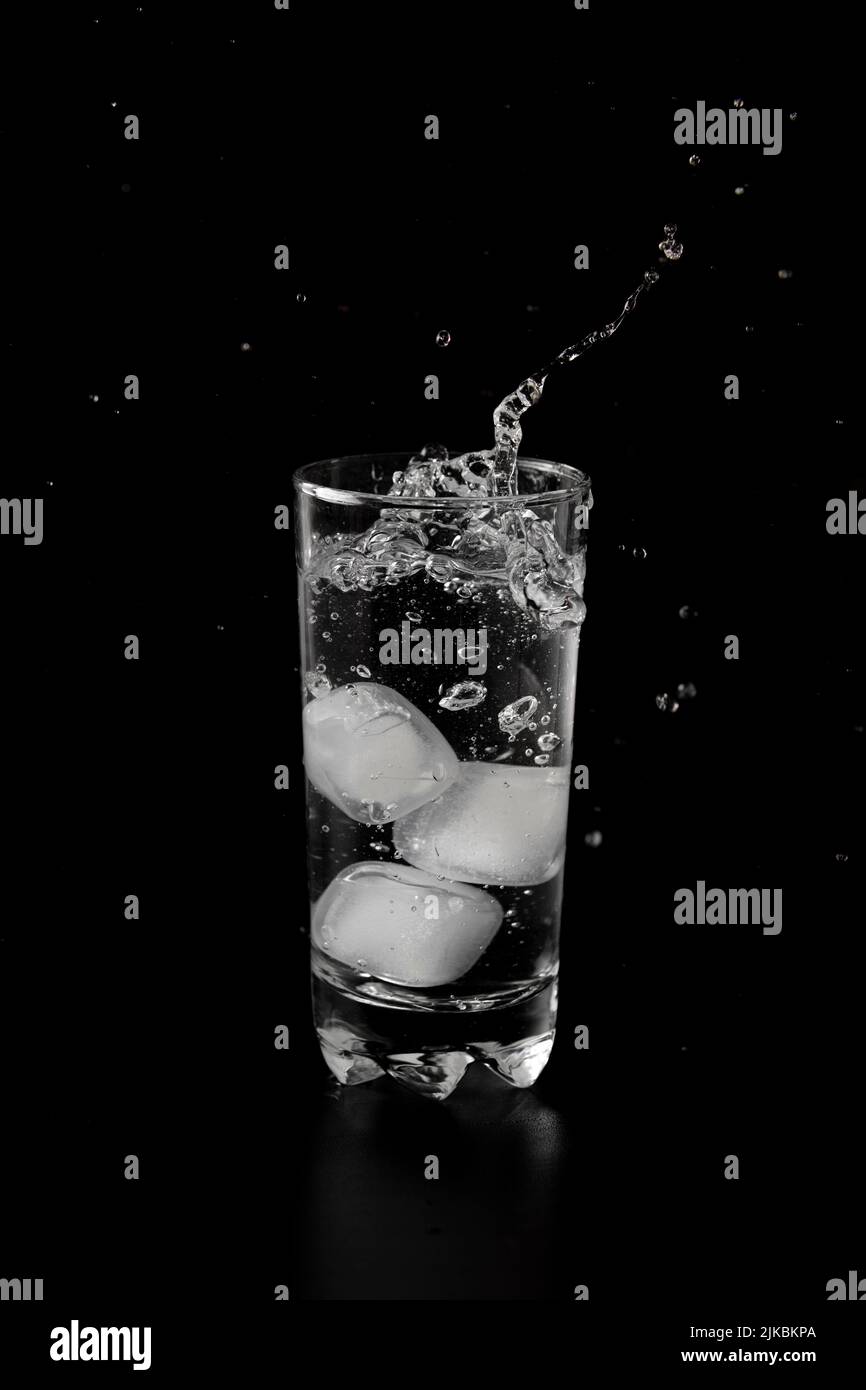 Ice cubes thrown to a glass of water from above with splash on a black ...