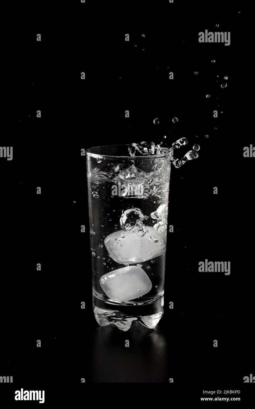Ice cubes thrown to a glass of water from above with splash on a black ...