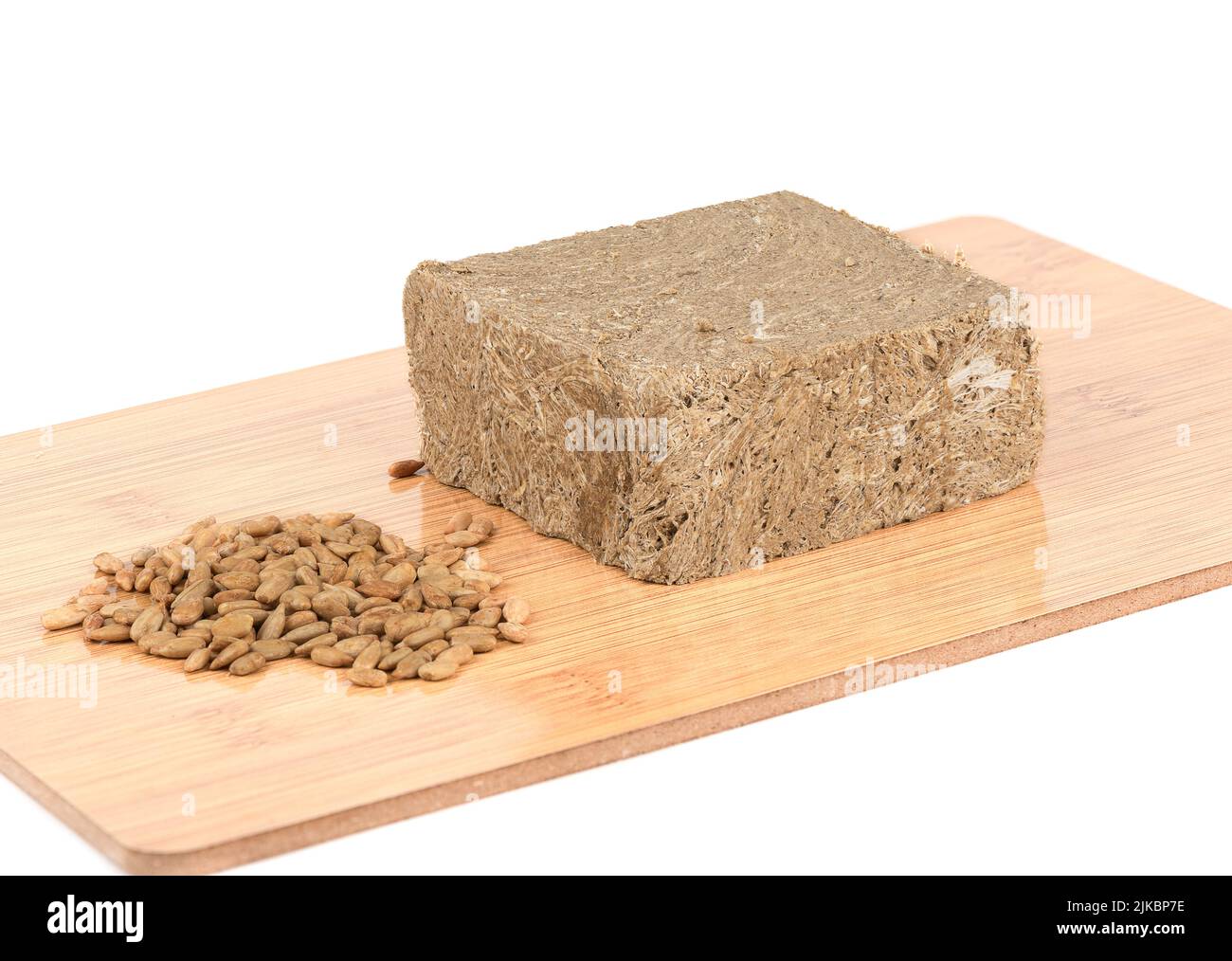 Sunflower halva and peeled sunflower seeds on a bamboo cutting board over a white background ...