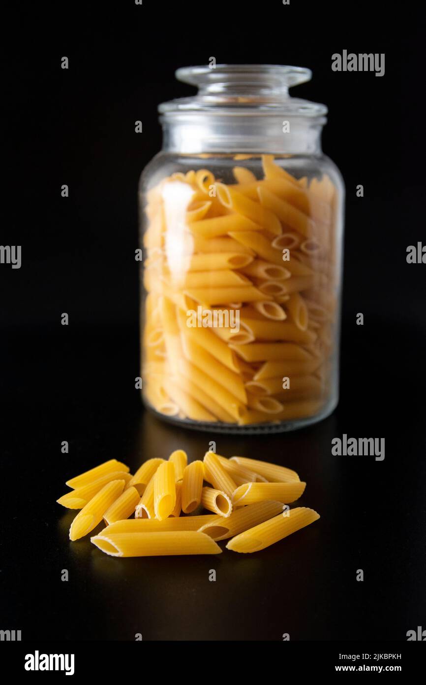 Penne pasta in front of glass jar on the black background Stock Photo ...