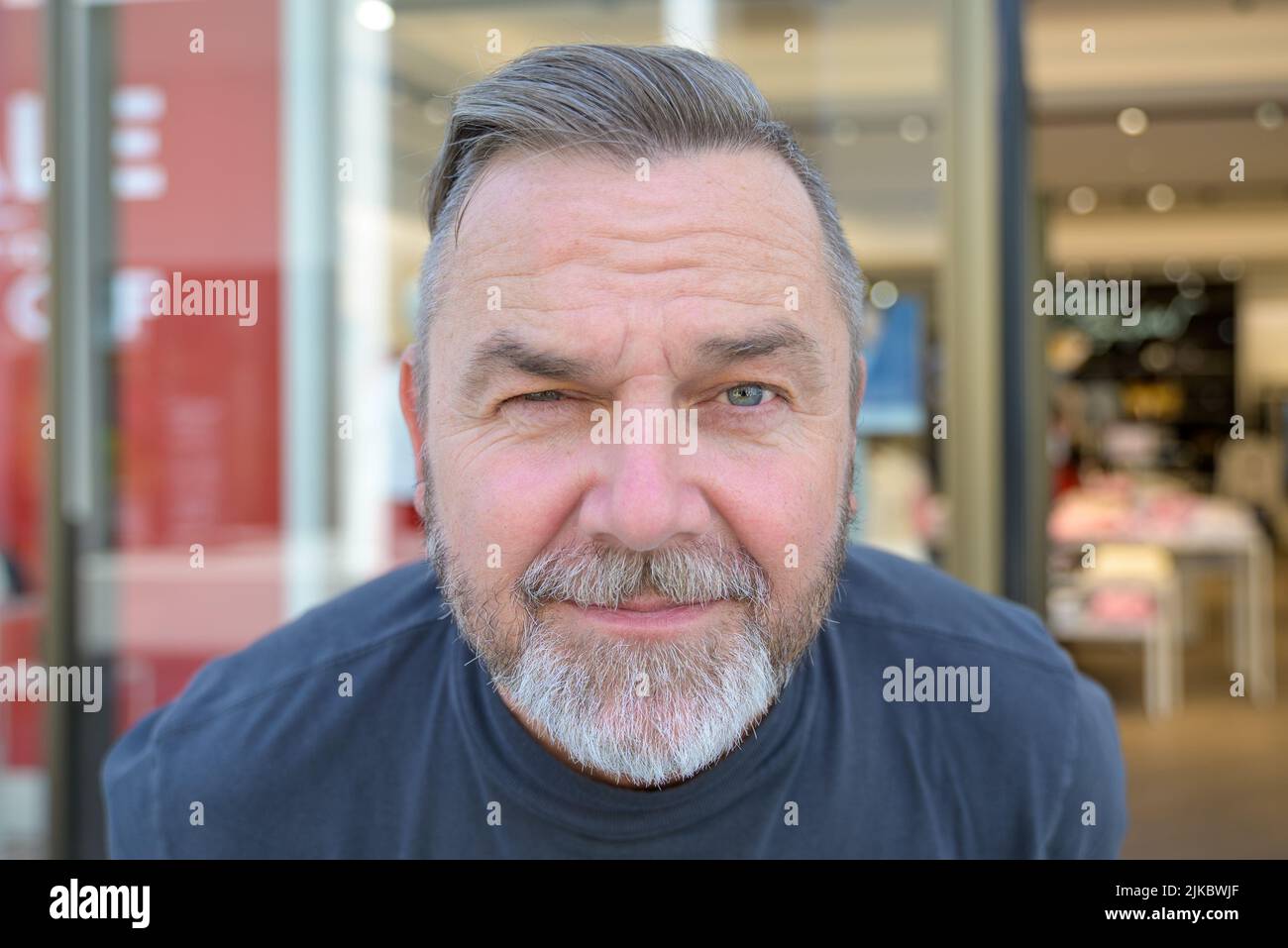 Senior man with a greying beard leaning forwards winking at the camera ...