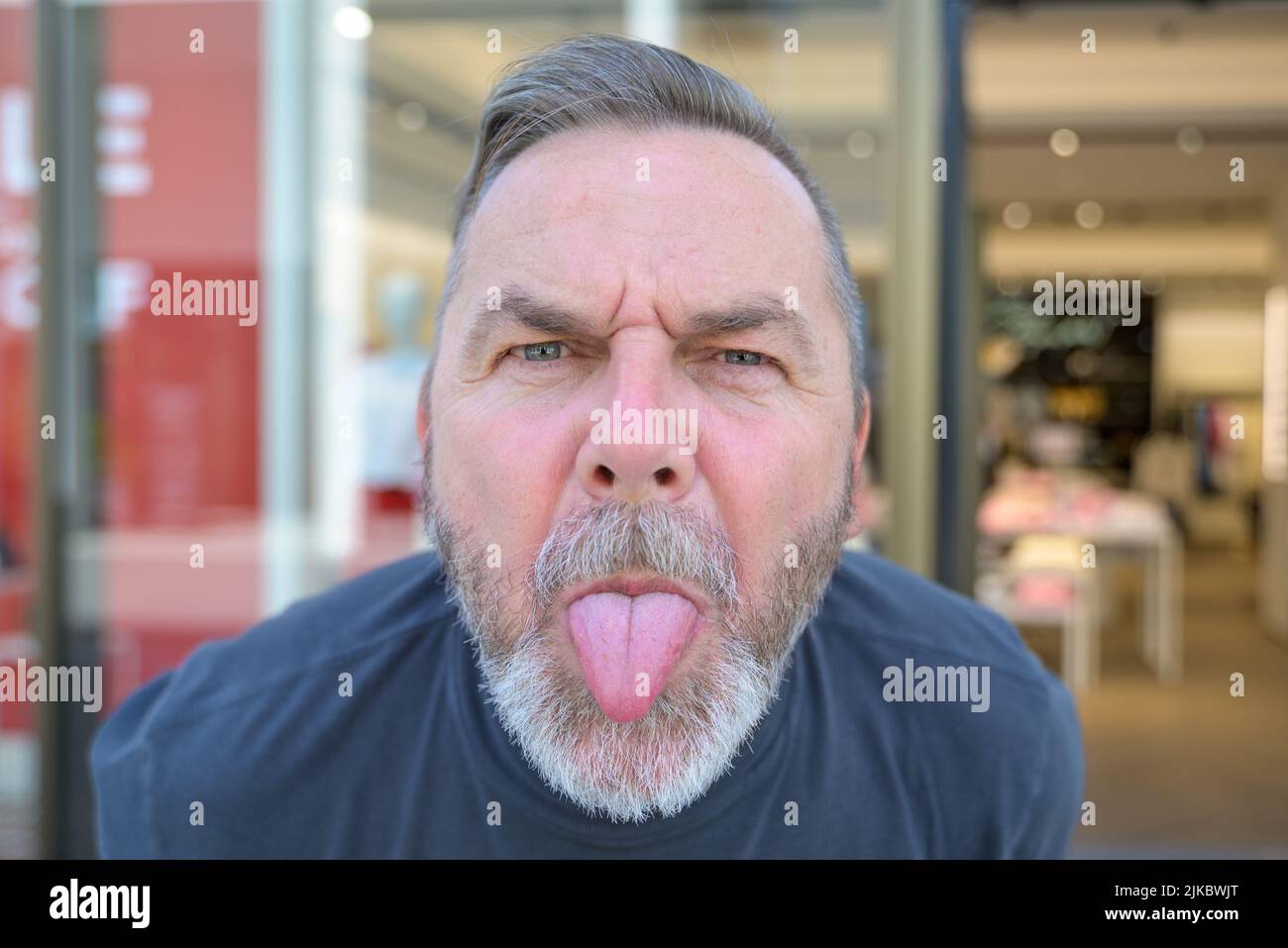 Childish rude man sticking out his tongue as he leans forwards towards ...