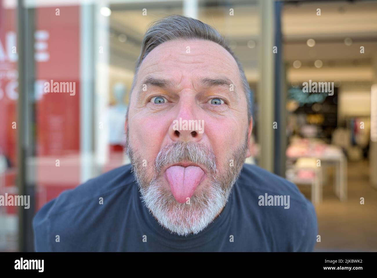 Childish rude man sticking out his tongue as he leans forwards towards the camera Stock Photo ...