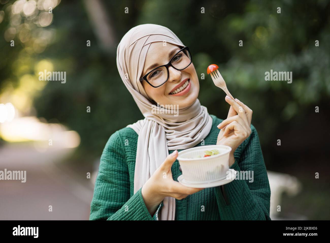 Happy positive muslim business woman eating healthy salad on a break ...