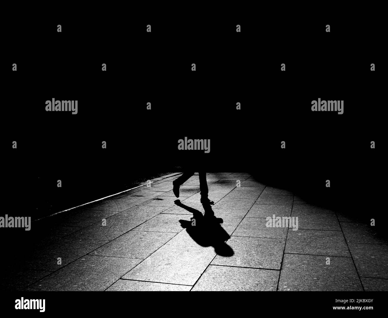 A silhouette of a walking man with a shadow of his body on the ground ...