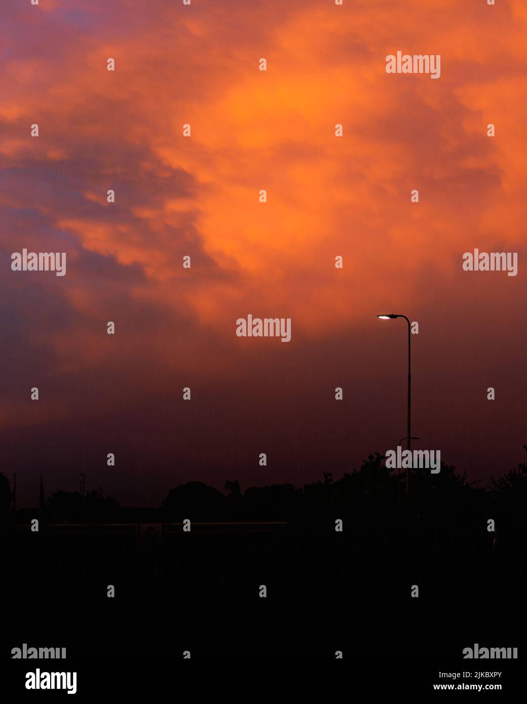 A bright red sky with clouds during the sunset with a street light pole ...