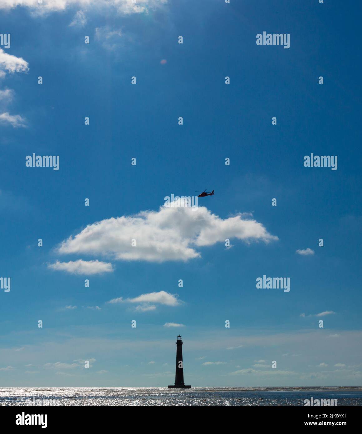 A vertical shot of the calm sea with a lighthouse under the clear blue ...