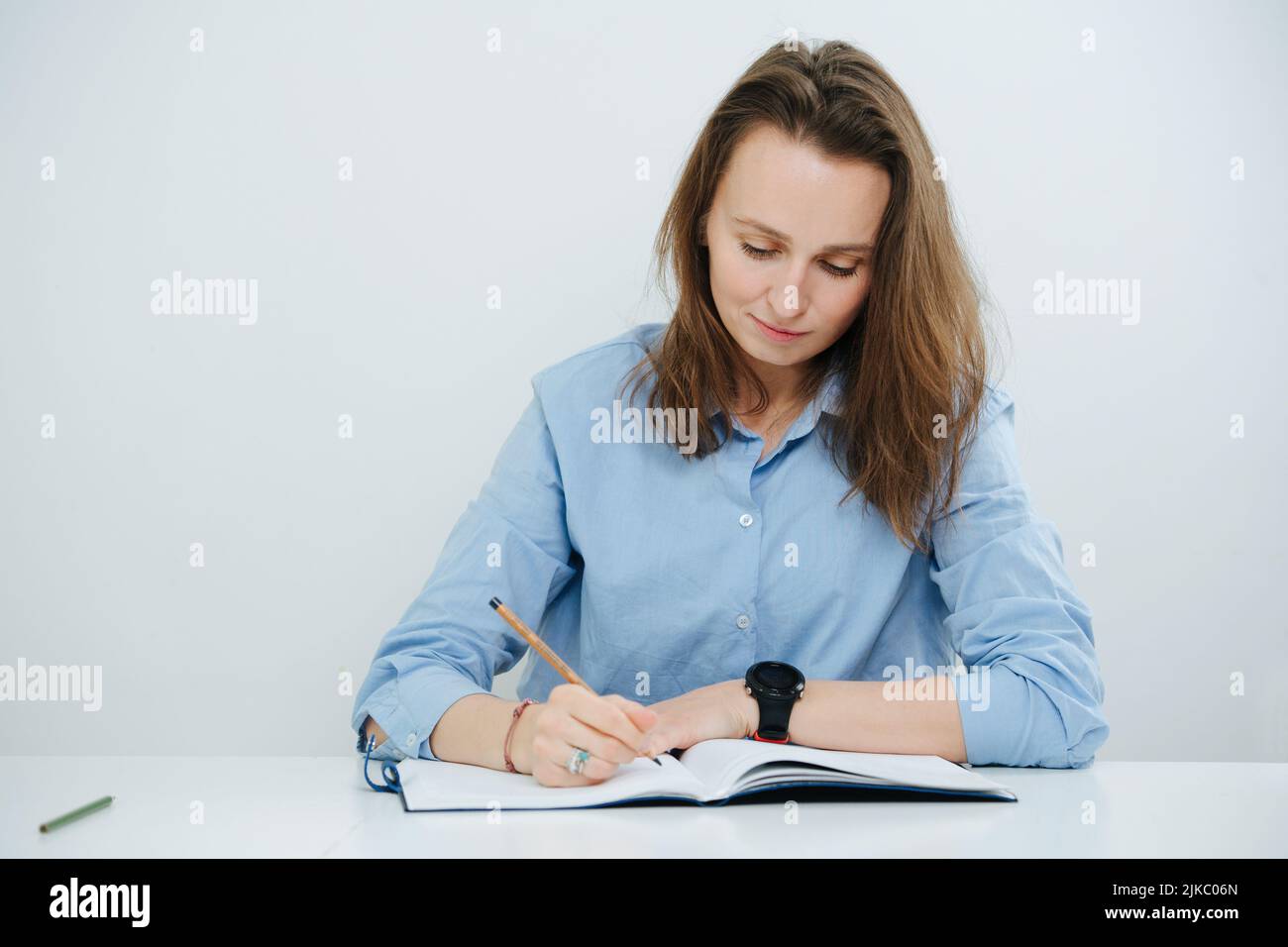 Diligent smirking business woman in blue dress shirt writing in a ...