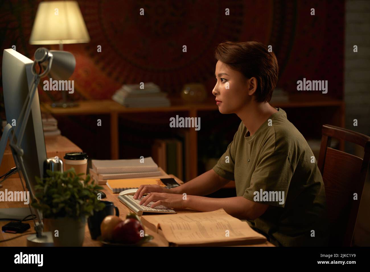 Side view of female Asian student typing on computer keyboard while ...