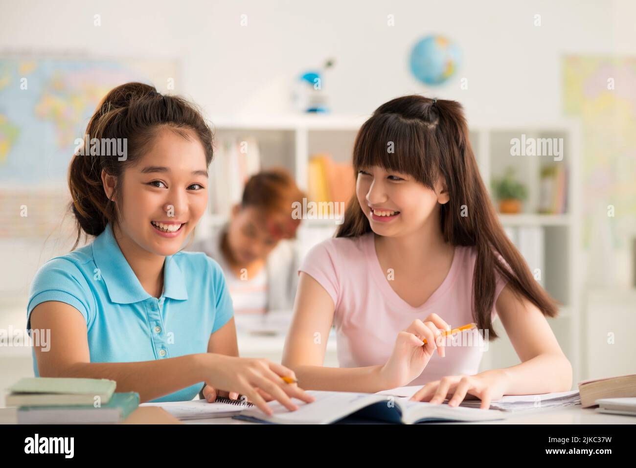 Cheerful teenage students having fun while sitting at desk and doing ...