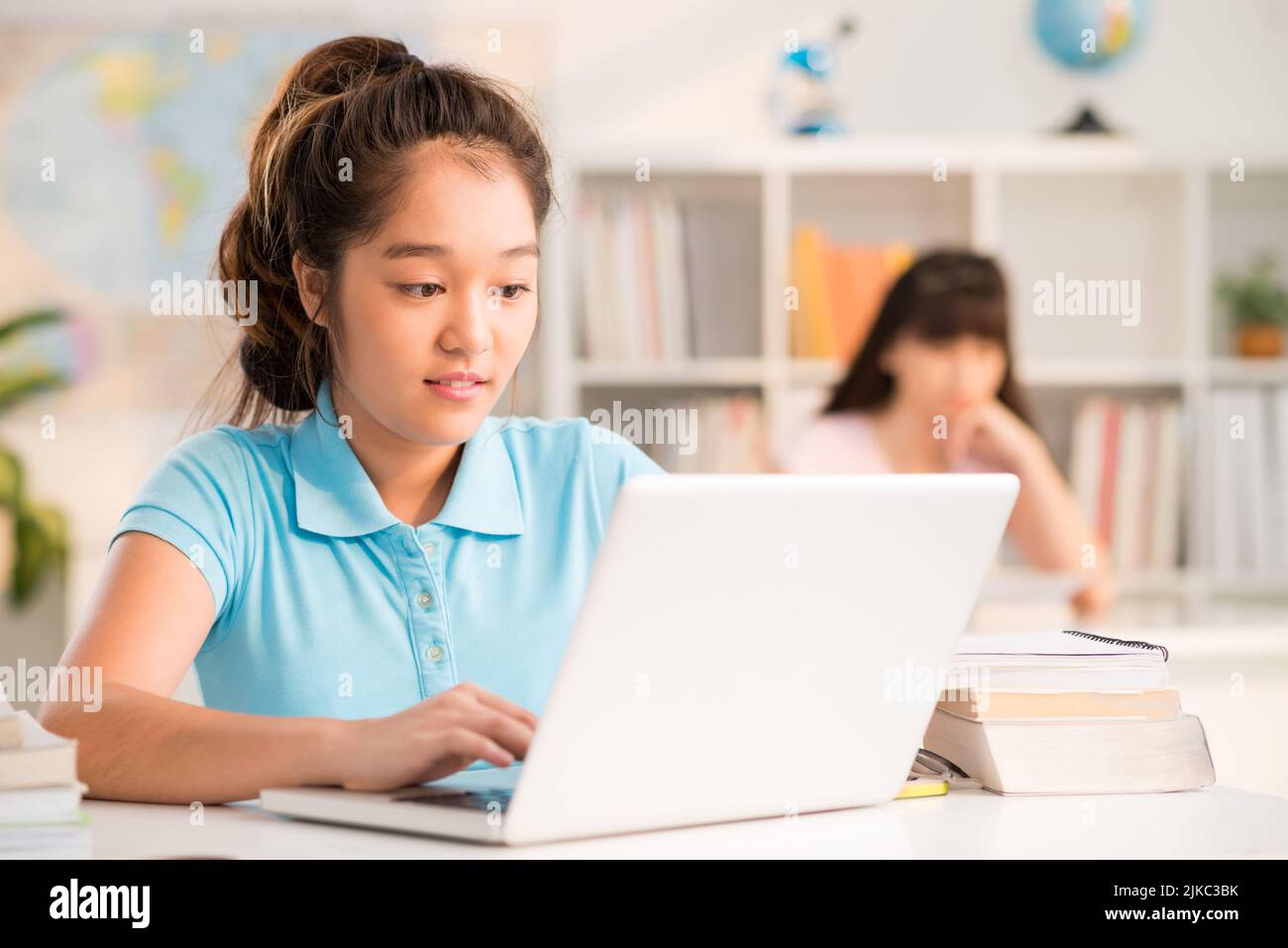 Pretty teenage student doing school project with help of laptop while ...