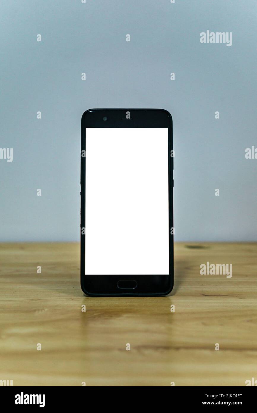A vertical shot of a smartphone on the table with a white screen for ...