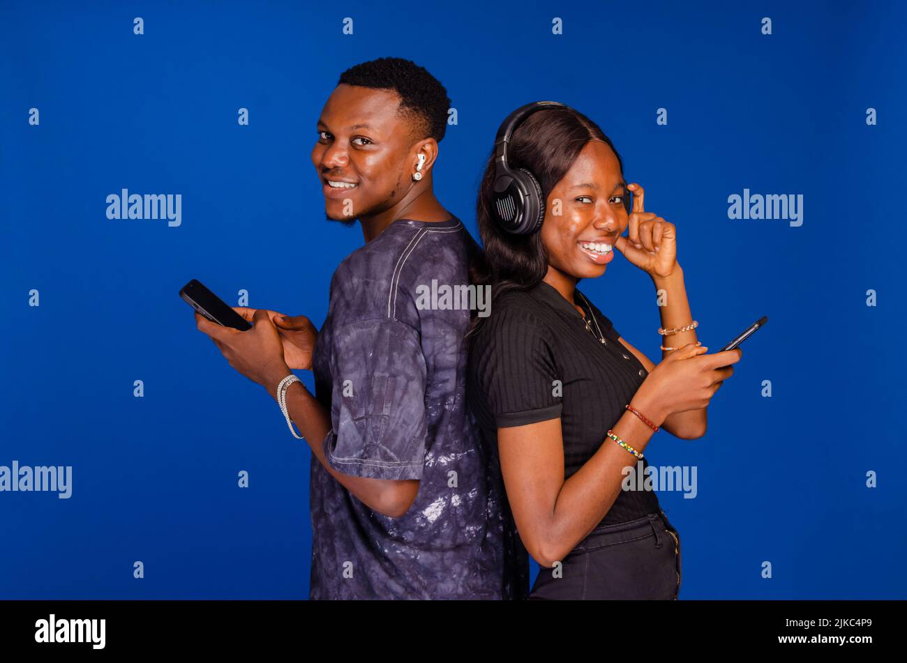 Positive african couple standing back to back, holding and using their ...