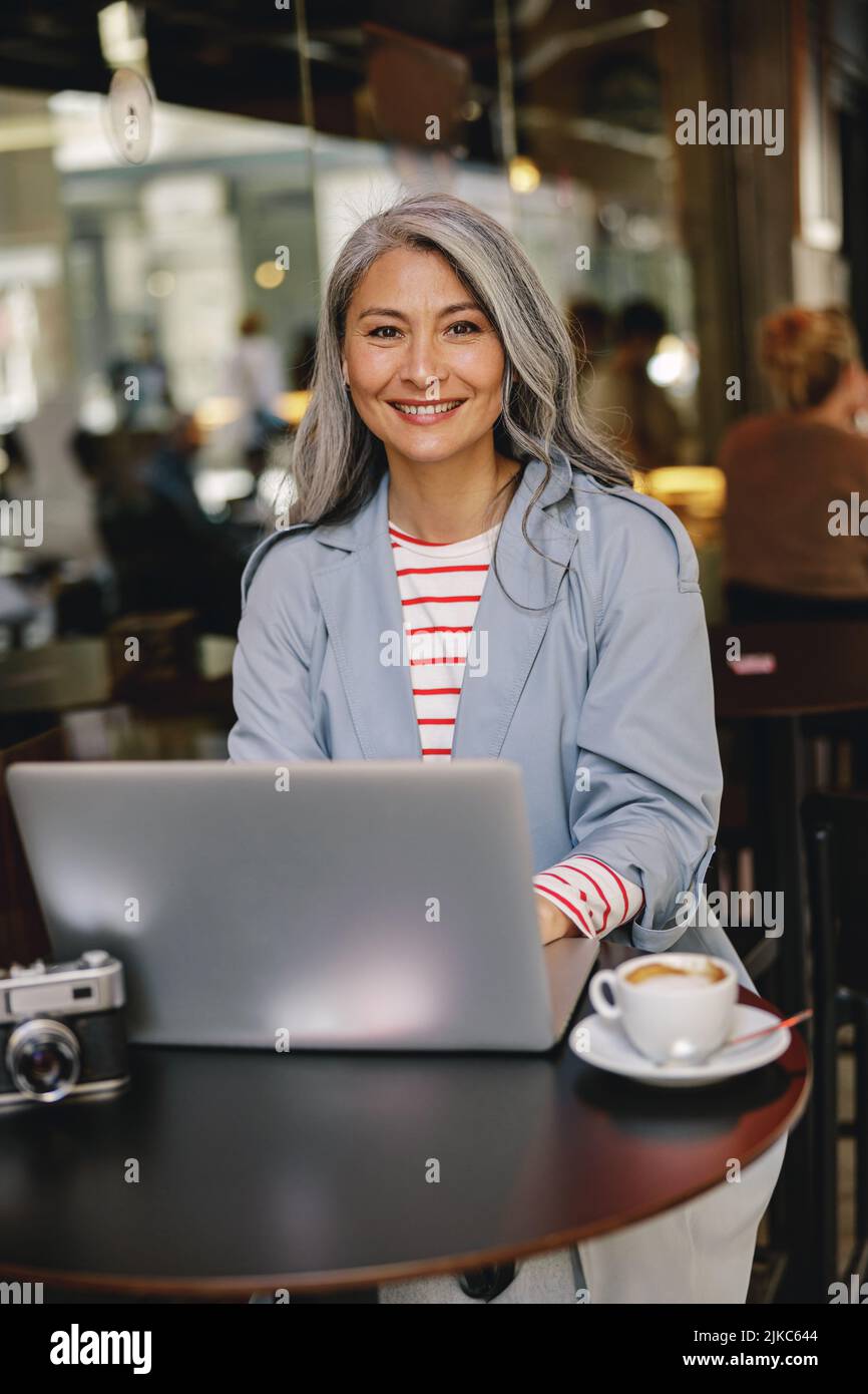 Happy mature lady working at city cafe Stock Photo - Alamy