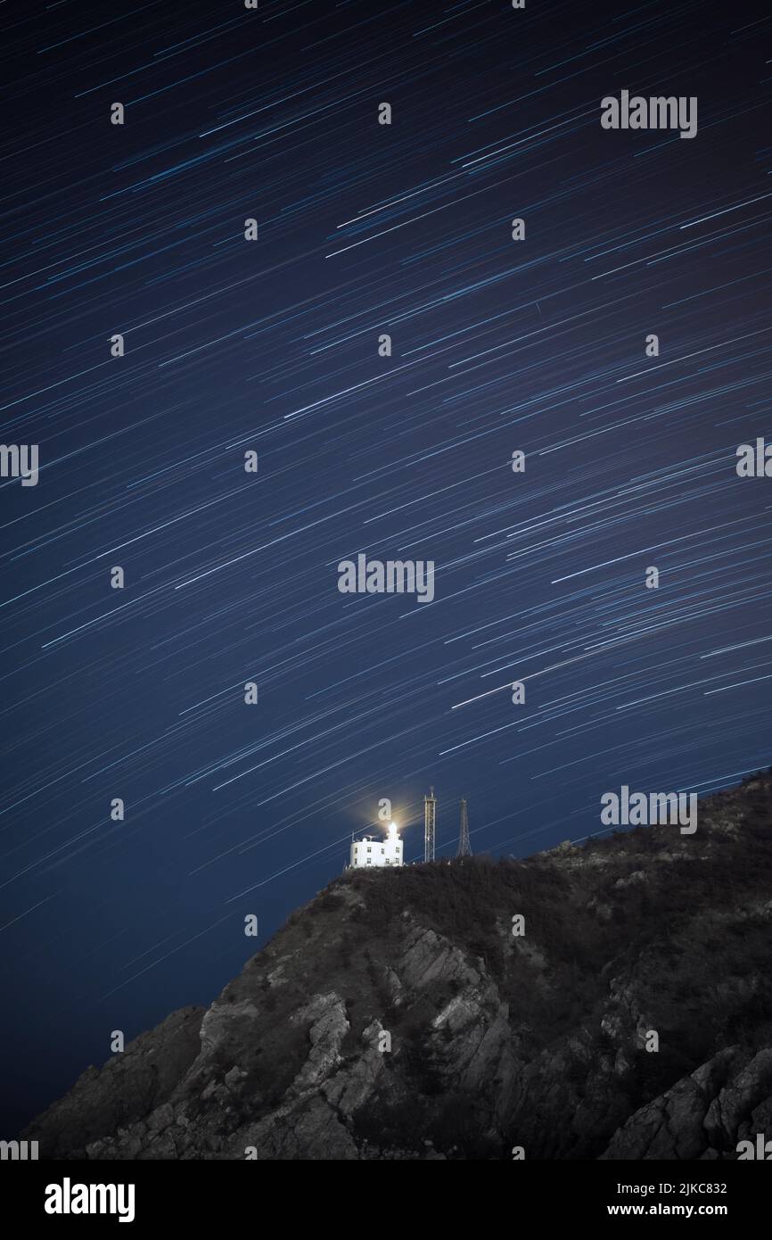 A vertical shot of star trails in sky over lighthouse on mountain Stock ...