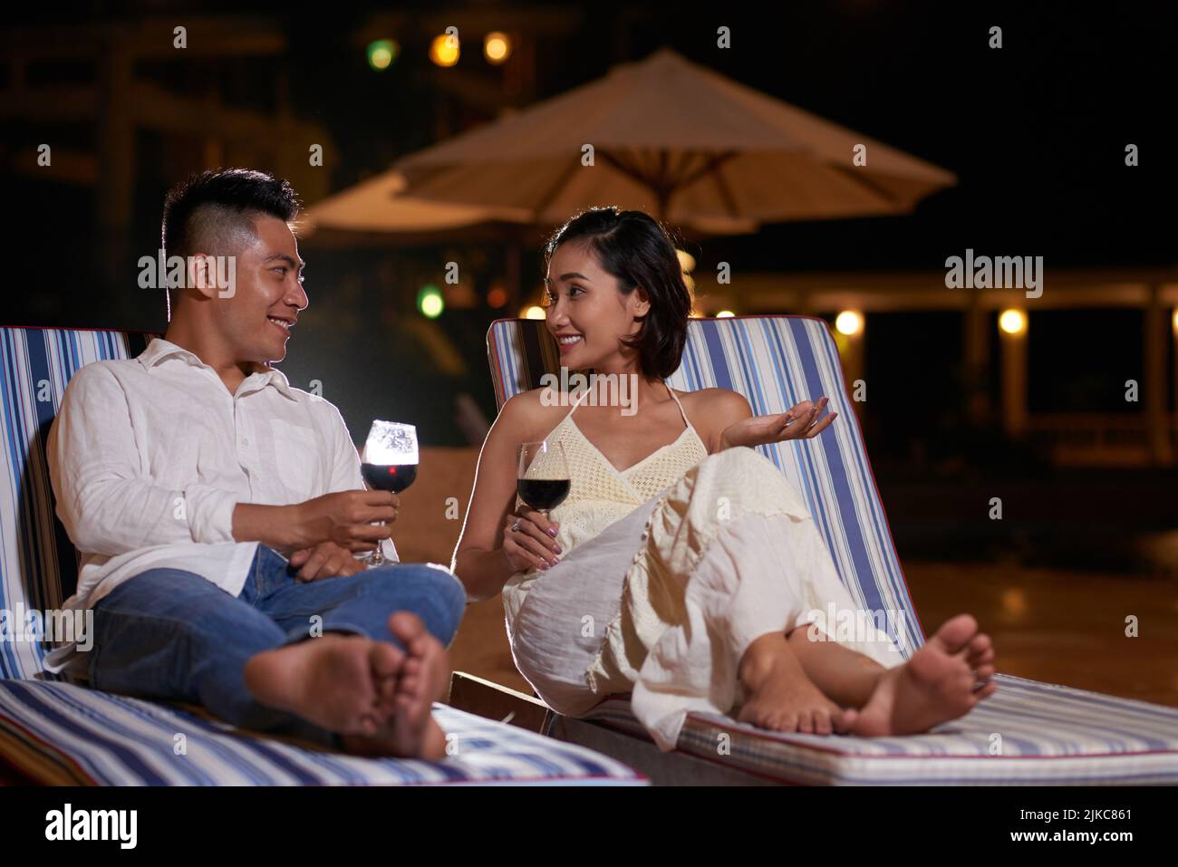 Smiling Asian woman sitting on deck chair with glass of red wine and ...