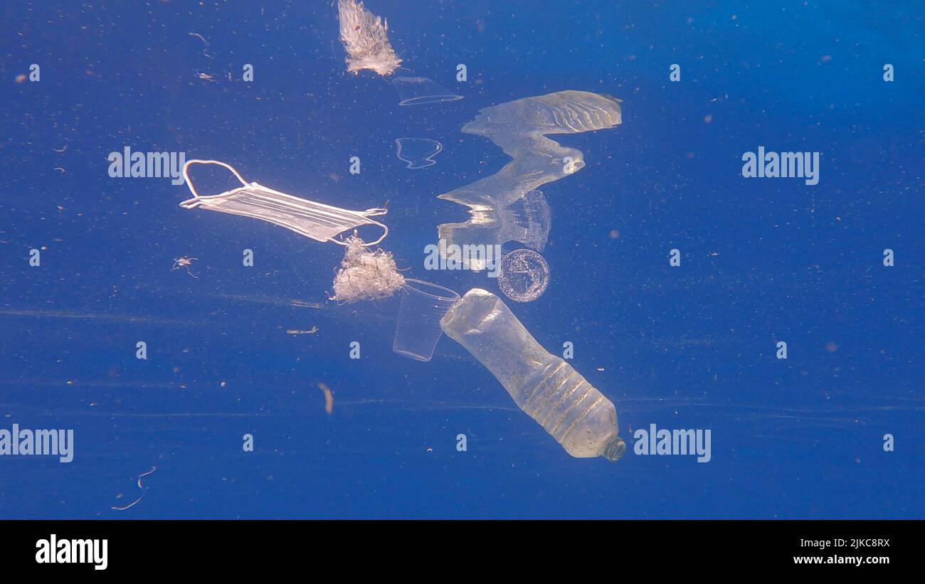Plastic bottle, cups and medical face mask swim in the blue water ...
