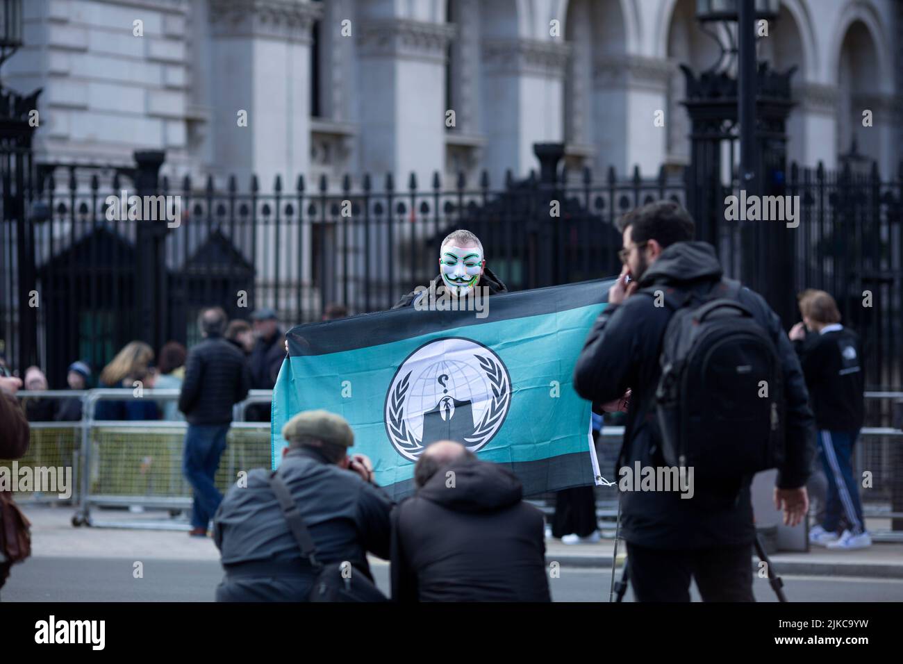 A person wearing a mask is surrounded by photographers during a Cost of ...