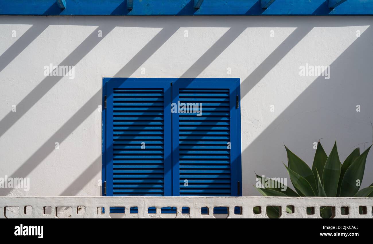 A blue window on the white-painted building with the shadow of fences ...