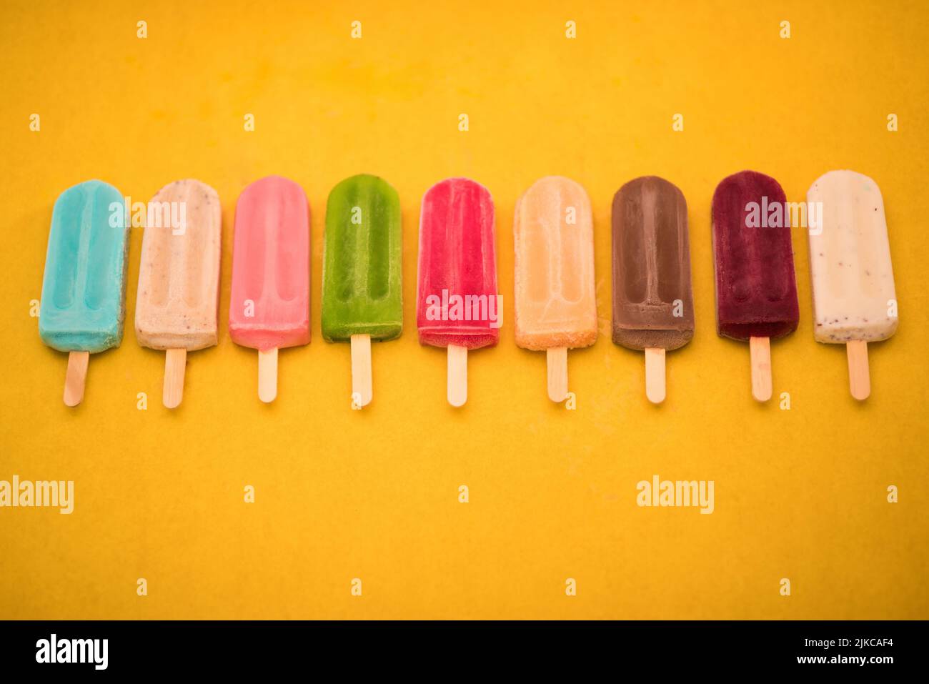A Top view of colorful ice cream bars in row on the yellow background ...