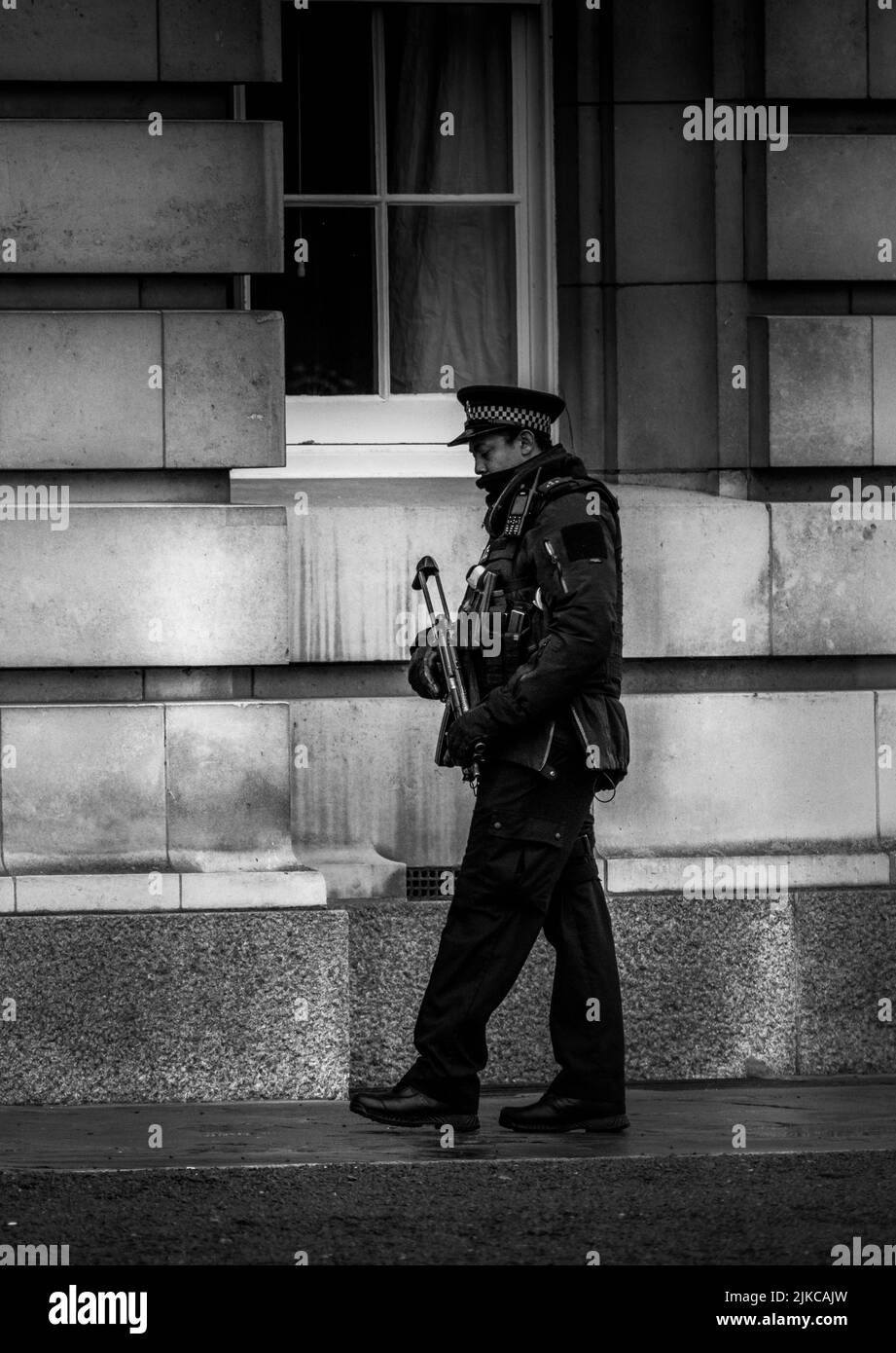 A vertical of a Caucasian policeman walking against Buckingham palace ...