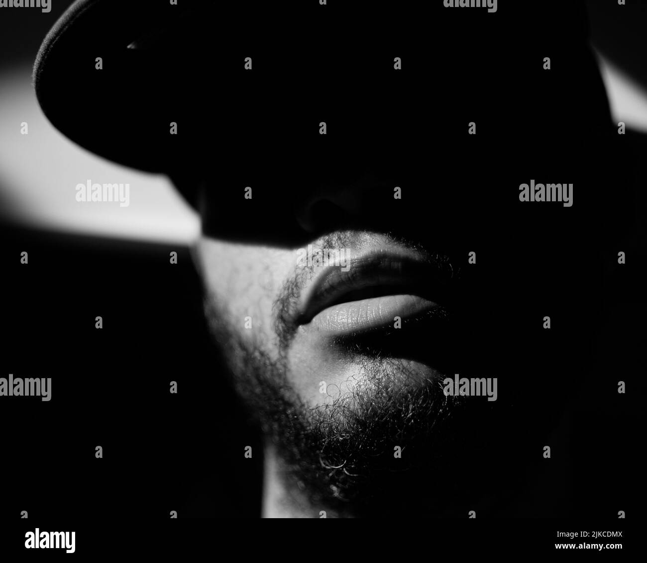 A grayscale portrait of a man in a baseball cap with shadow on his eyes ...