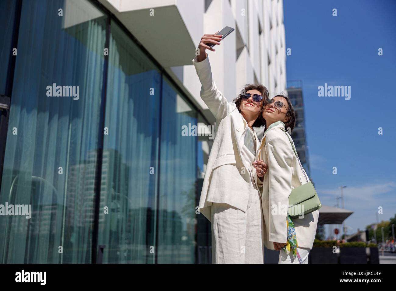 Two smiling woman in trendy outfits making selfie on background of ...