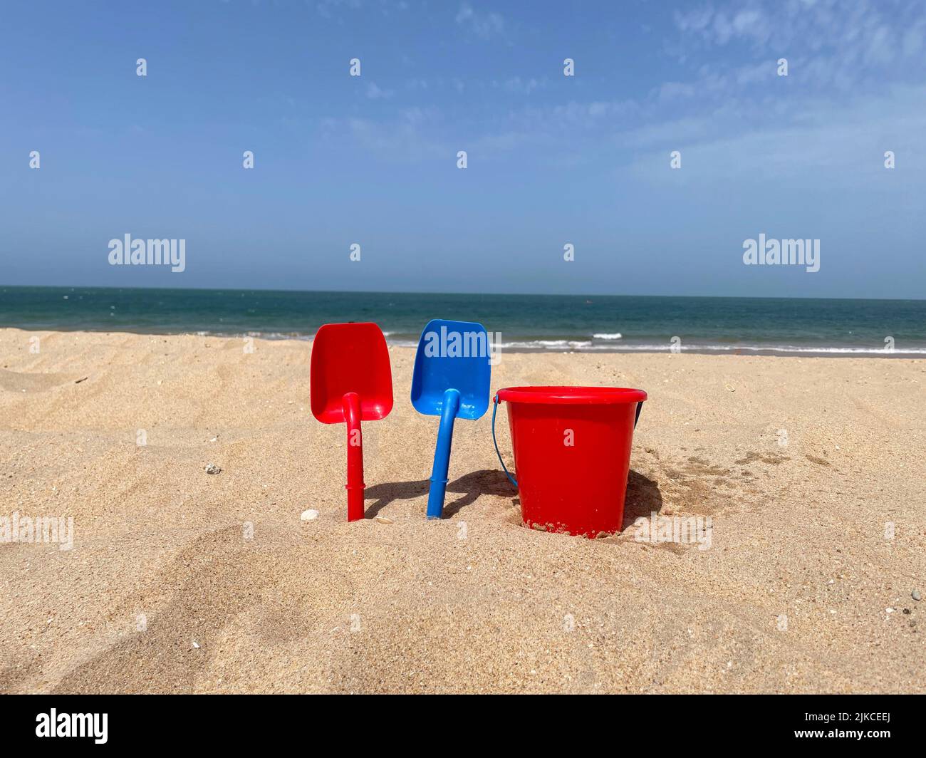 a view of a beach with red and blue plastic spades and a red bucket on ...