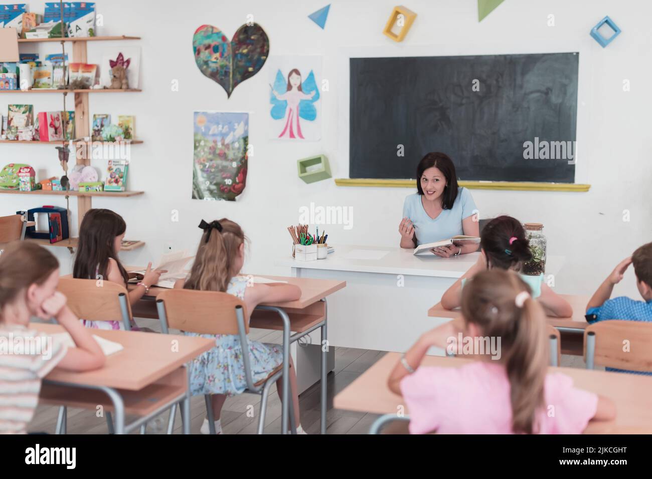 A teacher reads a book to elementary school students who listen ...