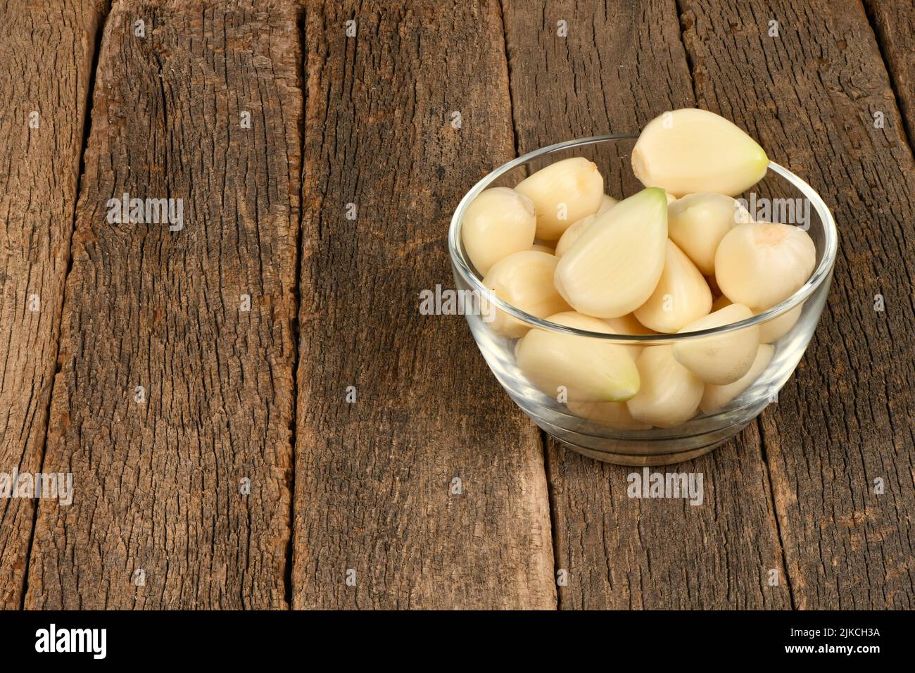 Pile of fresh garlic cloves in glass bowl, isolated on dark wood ...