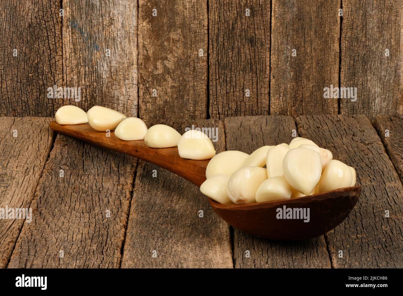 Pile of fresh garlic cloves in wooden spoon, isolated on dark wood ...