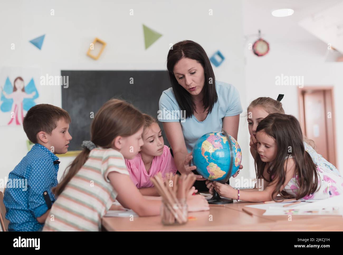 Female teacher with kids in geography class looking at globe. Side view ...