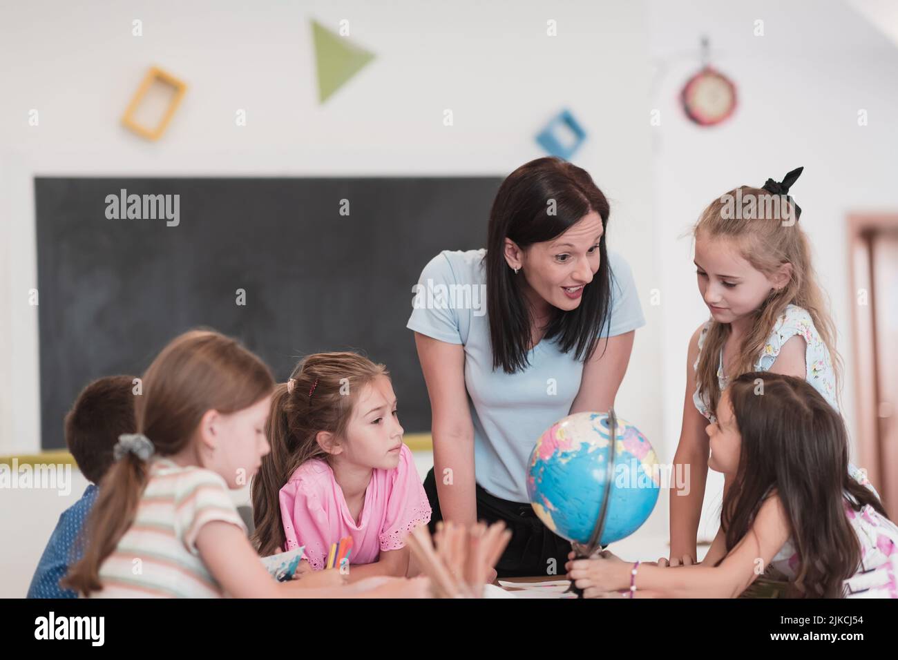 Female teacher with kids in geography class looking at globe. Side view ...