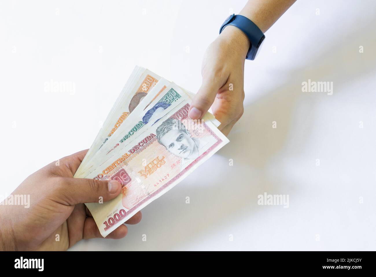 A closeup of a person handing cash Cuban peso bills to another person ...