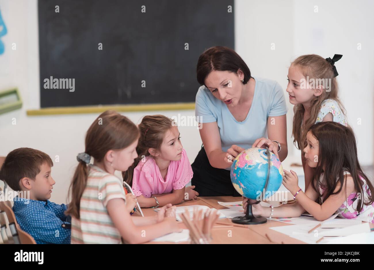 Female teacher with kids in geography class looking at globe. Side view ...