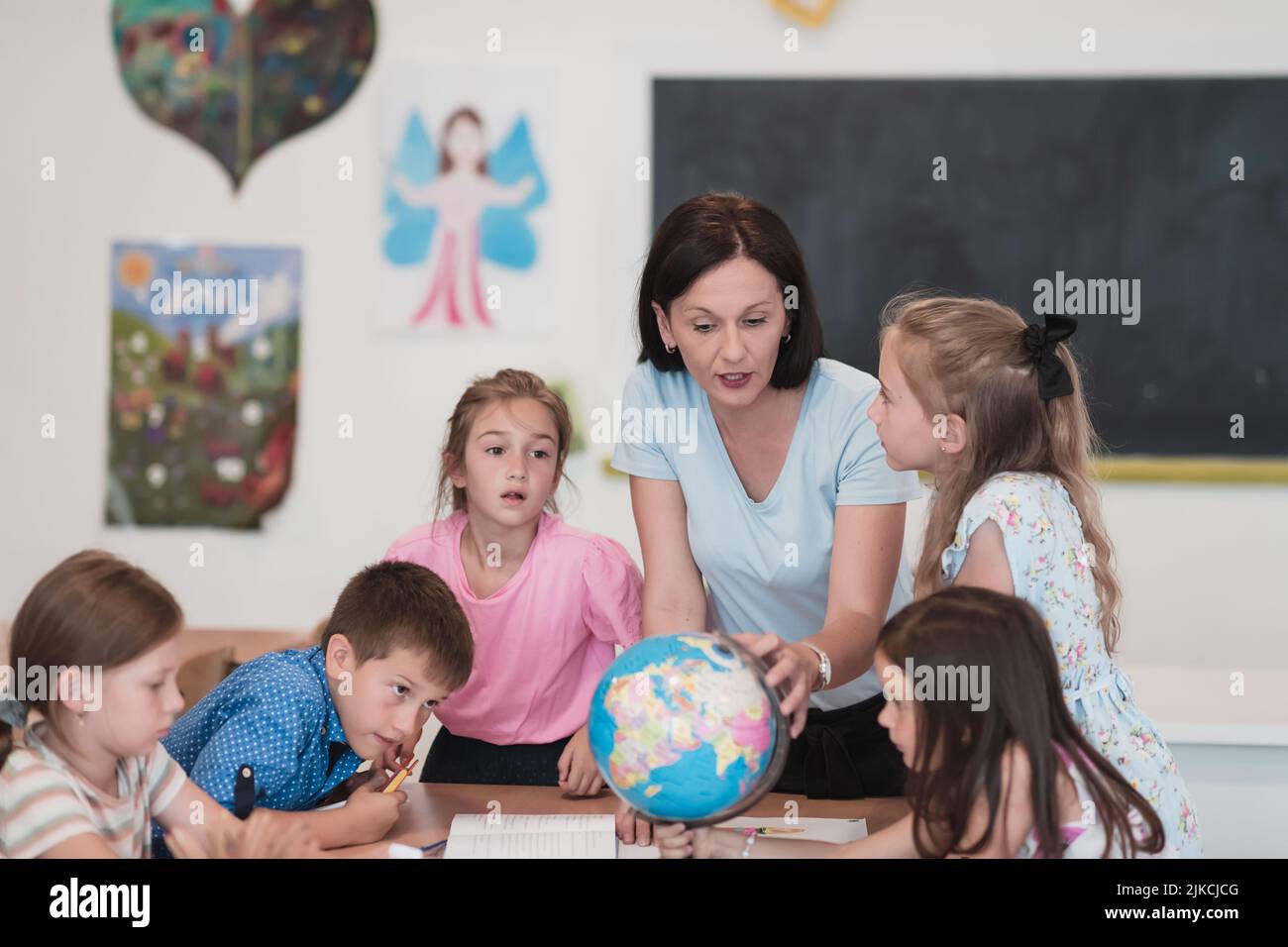 Female teacher with kids in geography class looking at globe. Side view ...