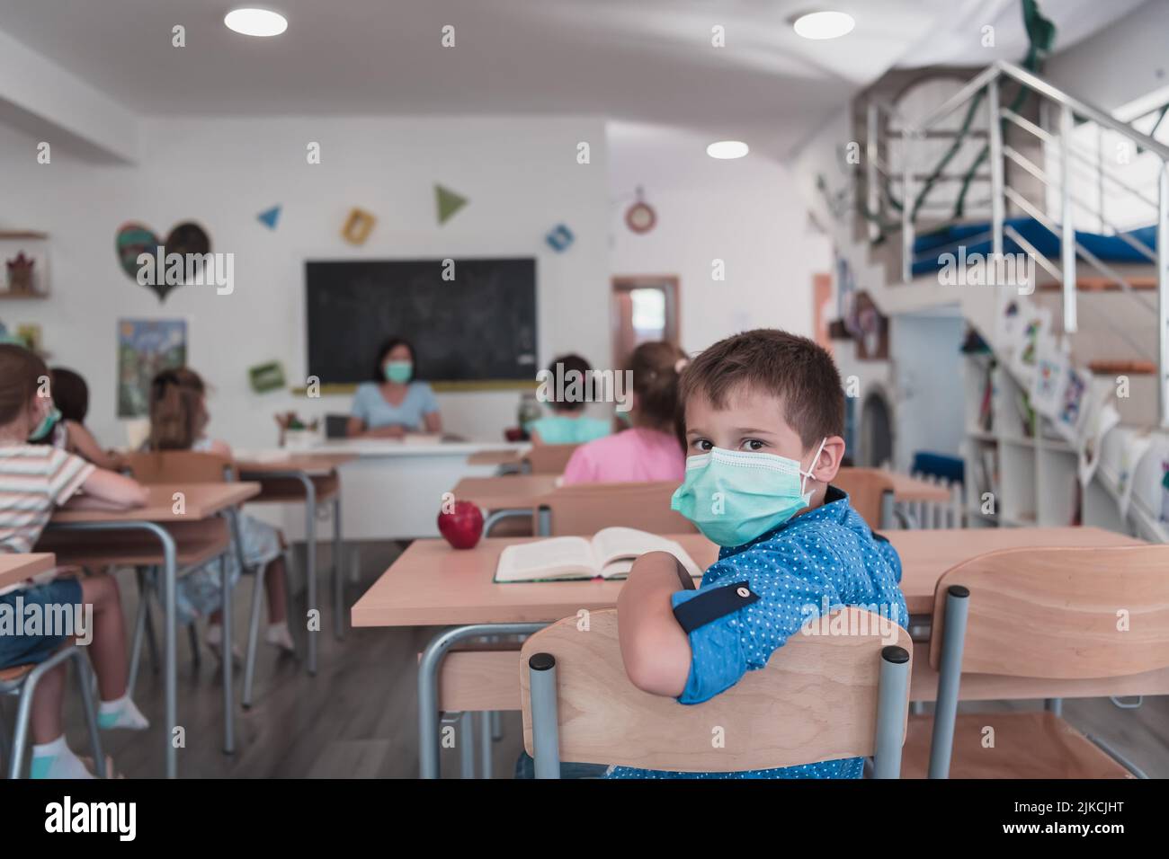 Multiracial group of kids wearing face masks working at class, writing ...