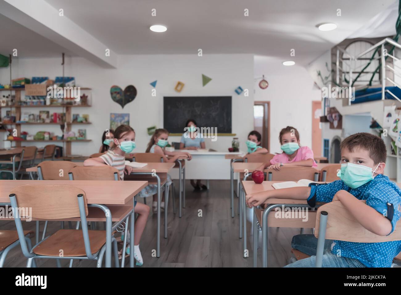 Multiracial group of kids wearing face masks working at class, writing ...